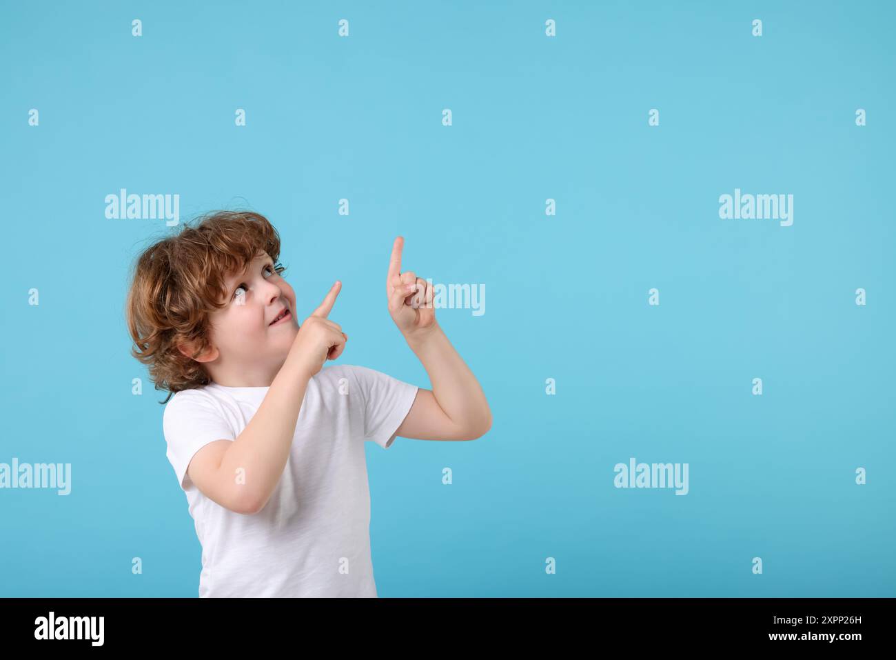 Cute little boy pointing at something on light blue background, space ...
