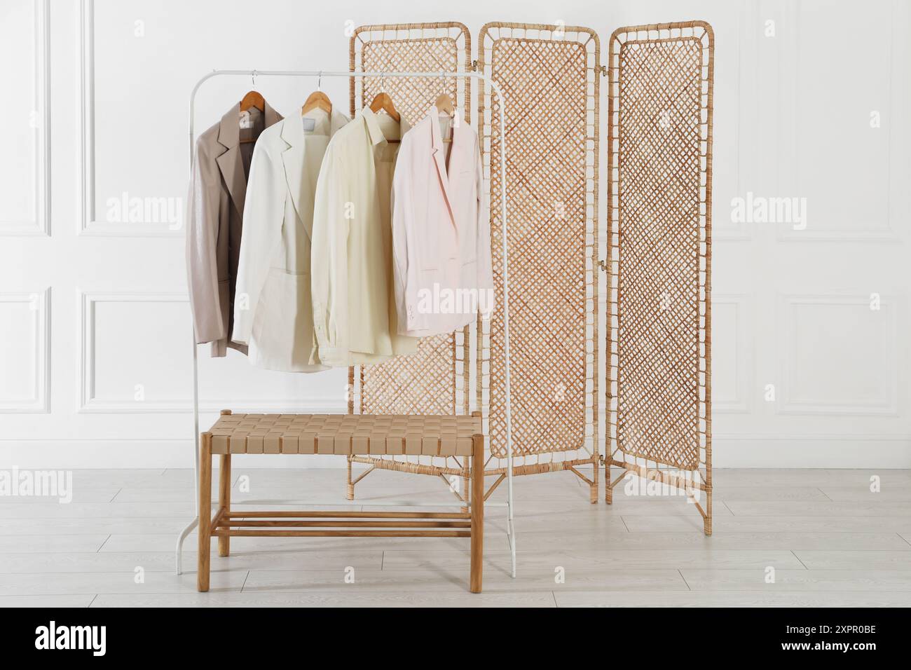 Folding screen, rack with clothes and storage bench near white wall ...