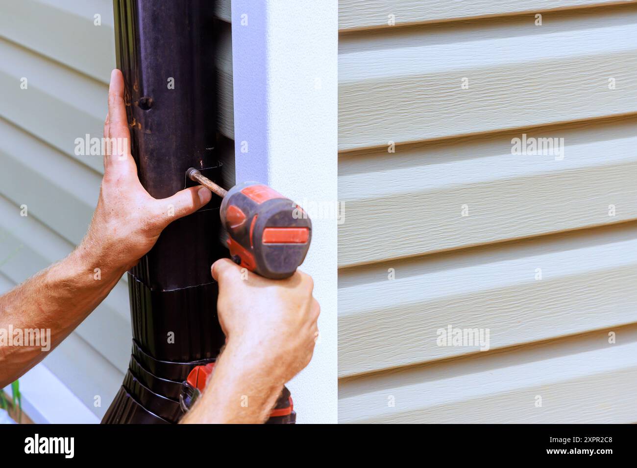 An employee installing rain gutter on roof with is installing downpipe ...