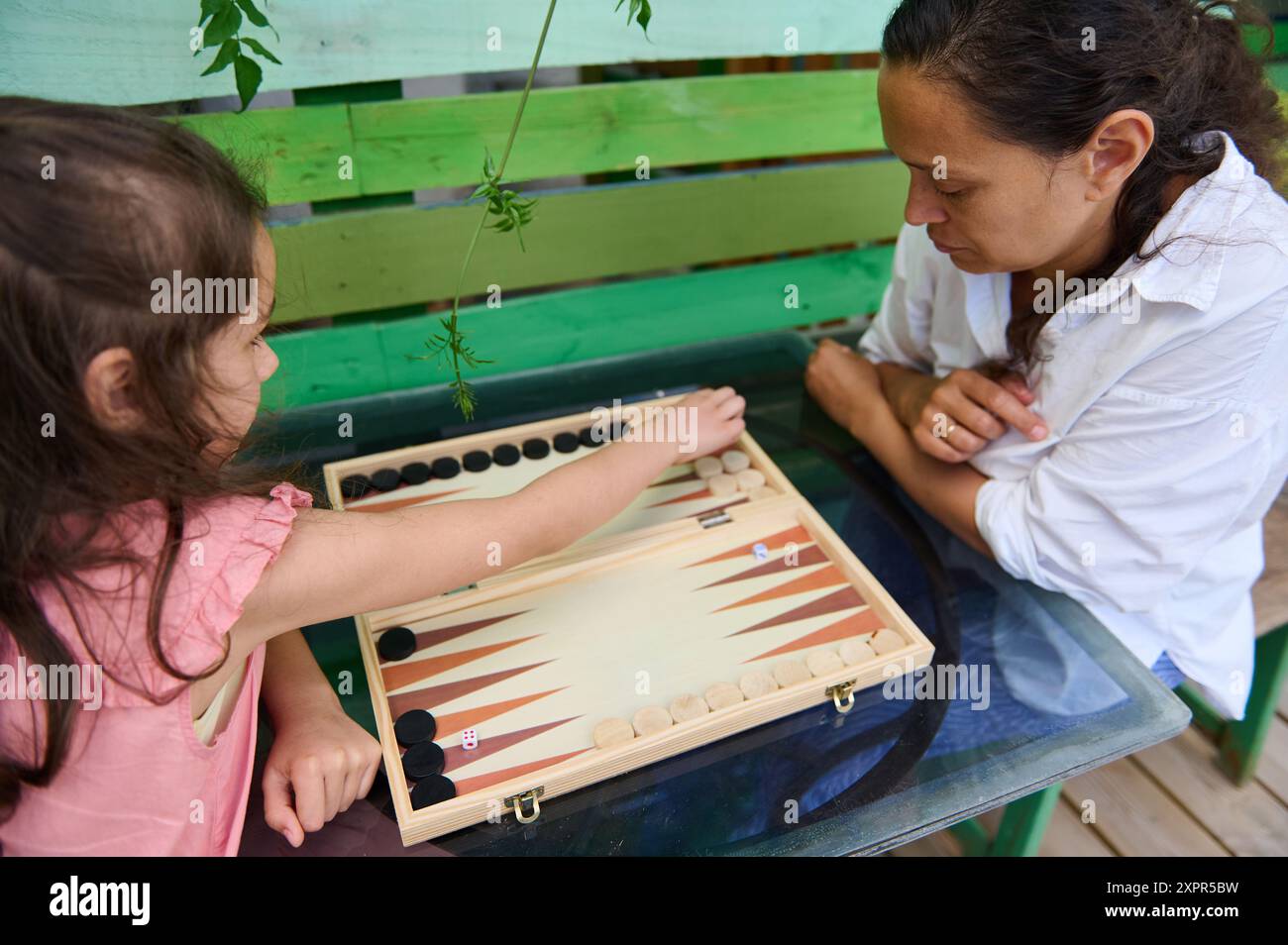 A woman and young girl engage in a backgammon game outside, enjoying ...