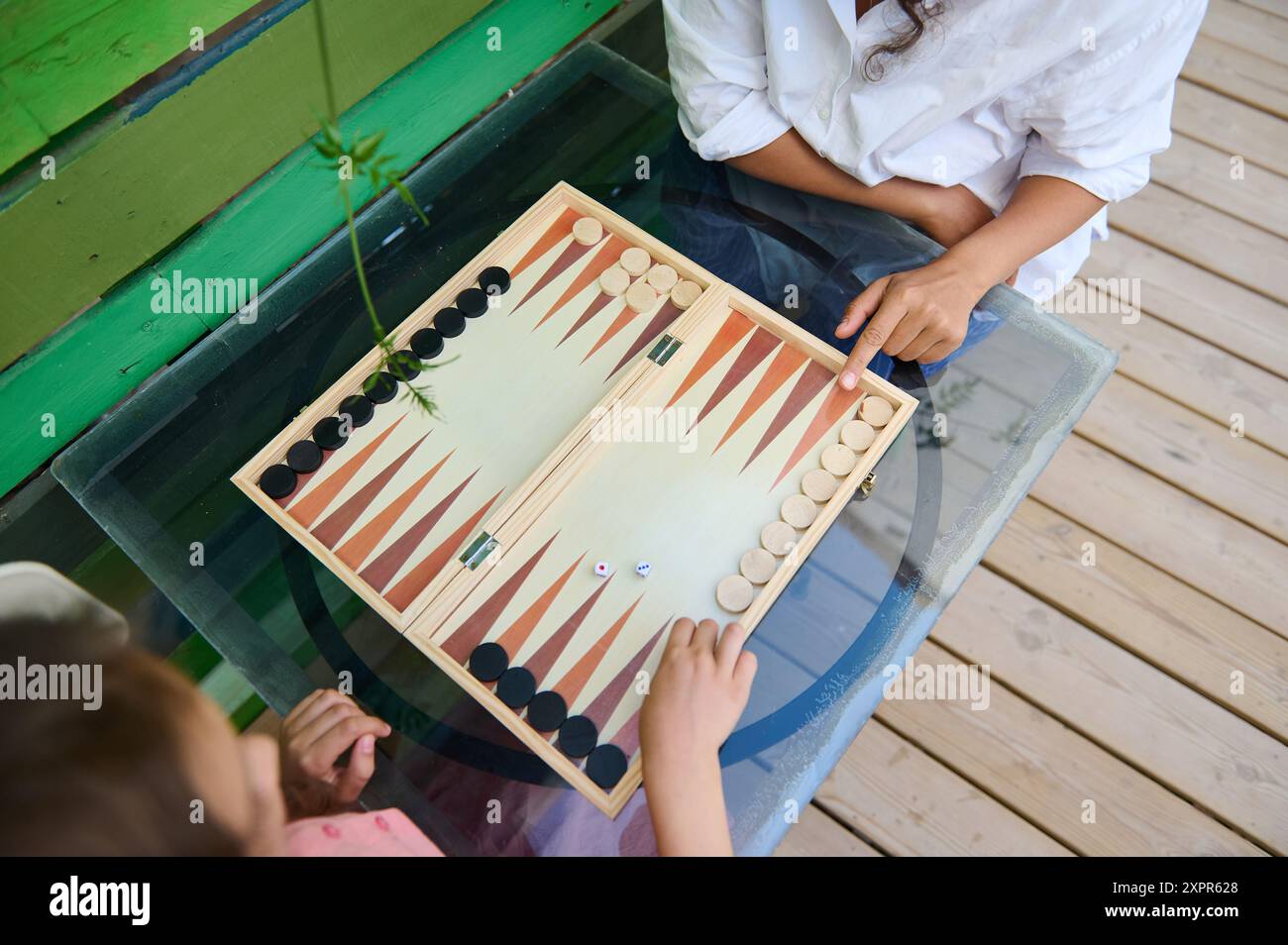 Two people playing backgammon outdoors at a glass table. Friends or ...