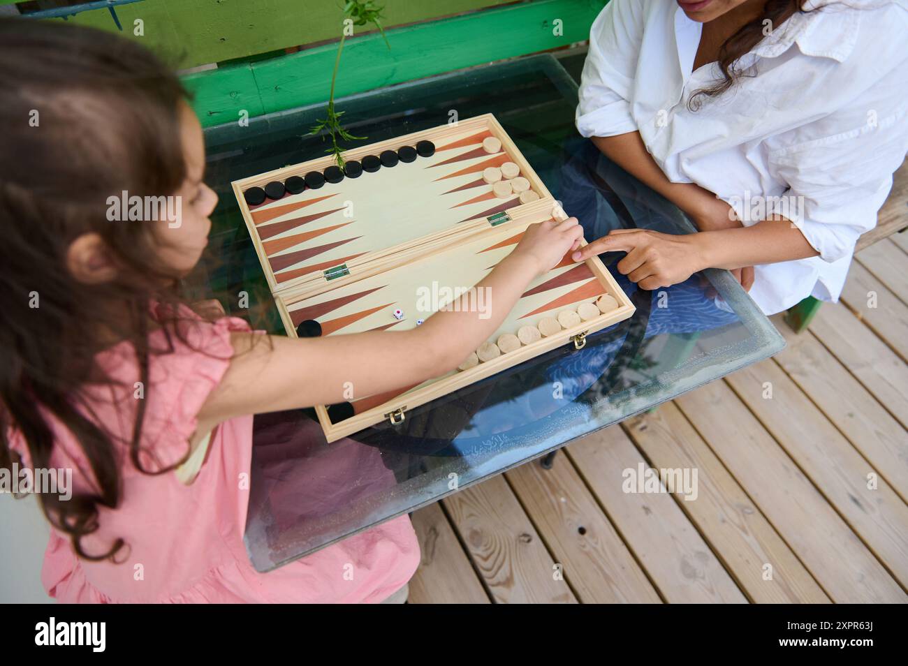 Mother and daughter playing backgammon on a glass table outside. A ...