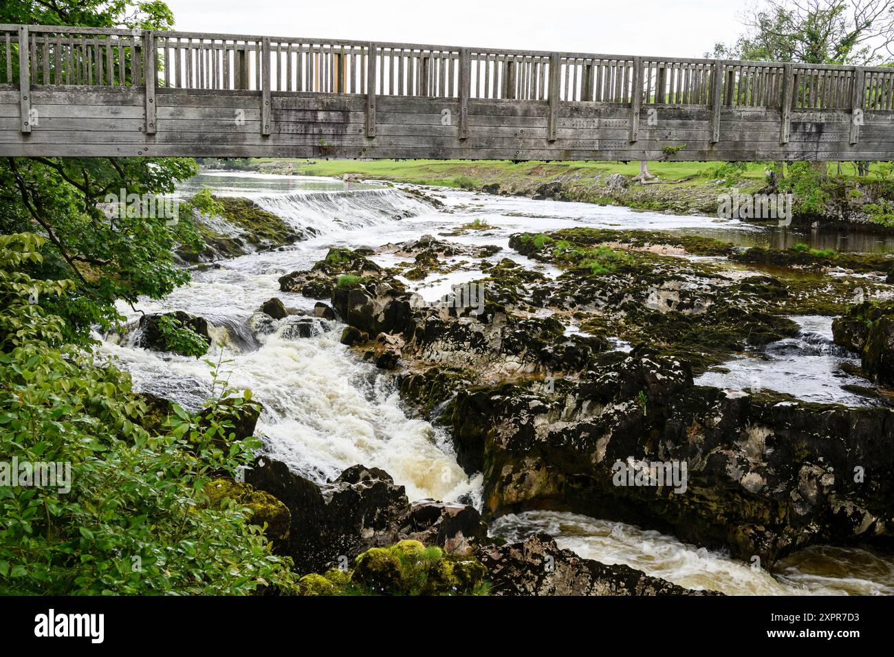 A rustic wooden bridge over a cascading river surrounded by lush ...