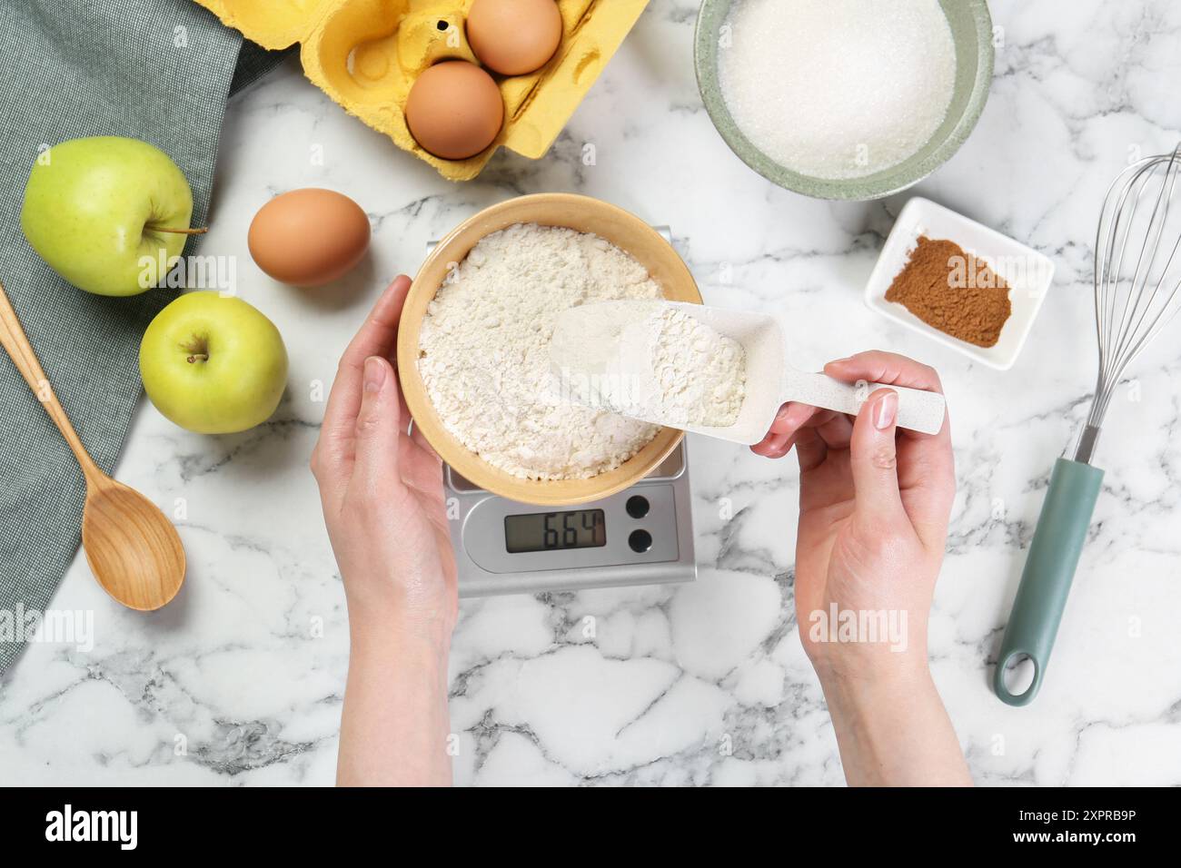 Woman adding flour into bowl on kitchen scale at white marble table ...
