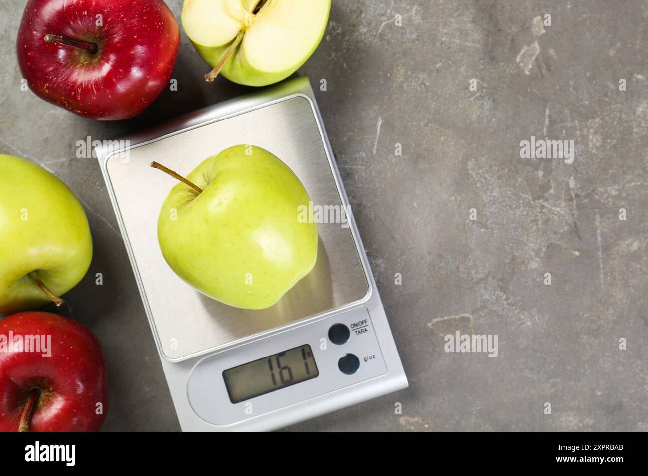 Kitchen scale with apple among ones on grey textured table, flat lay ...