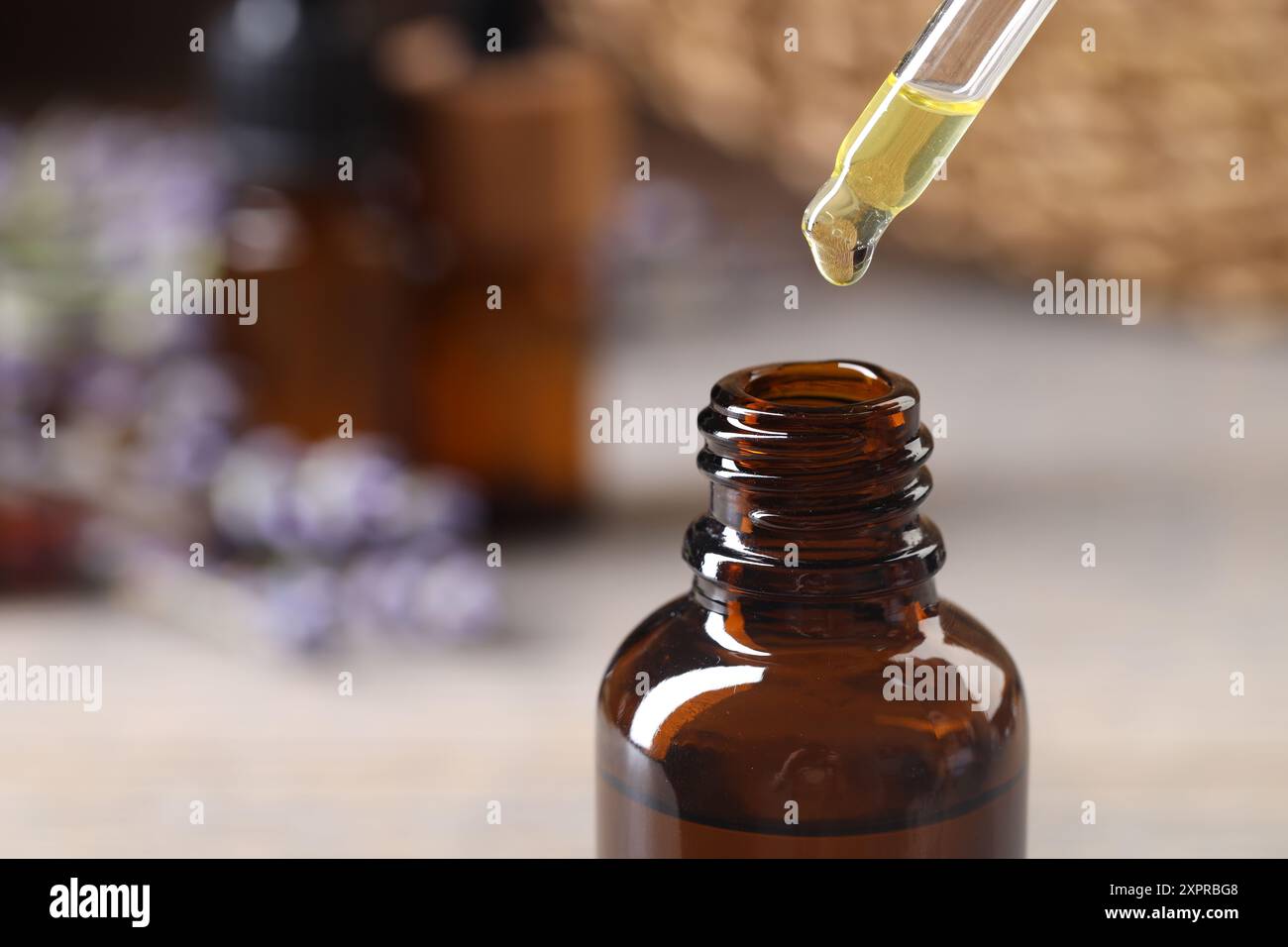 Essential oil dripping from pipette into bottle against blurred ...
