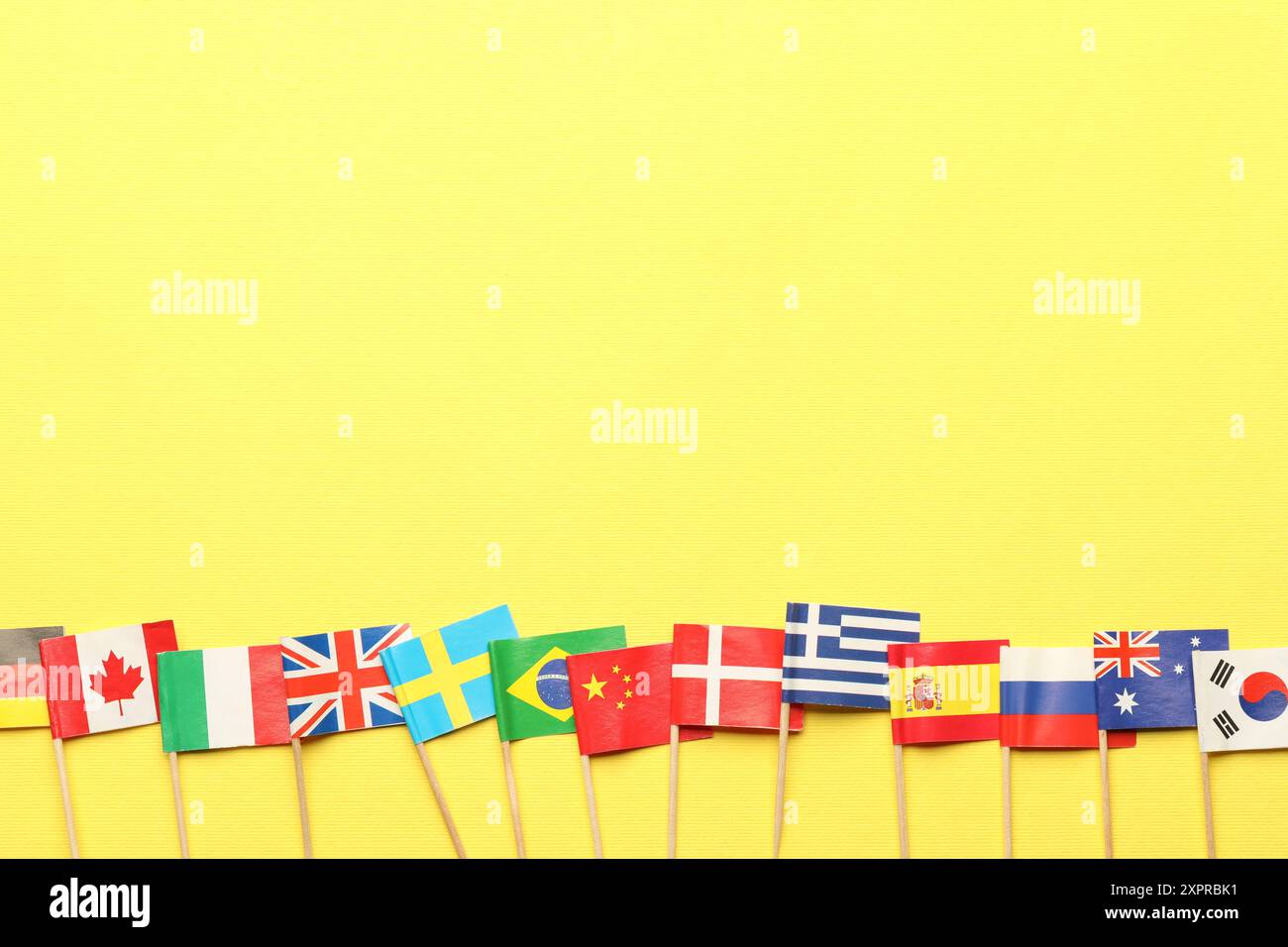 Small paper flags of different countries on yellow background, flat lay ...