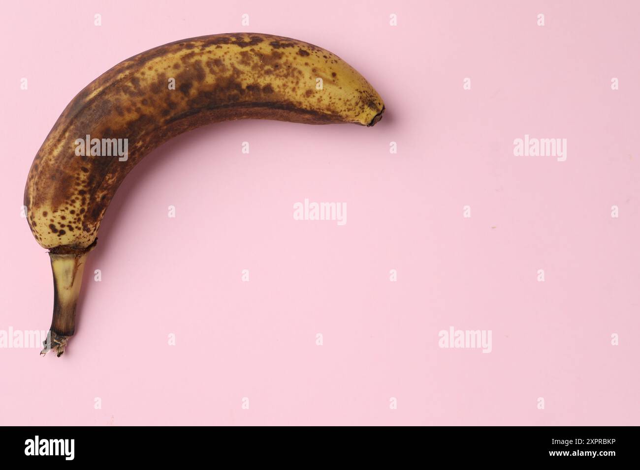 Overripe banana with dark spots on pink background, top view. Space for ...