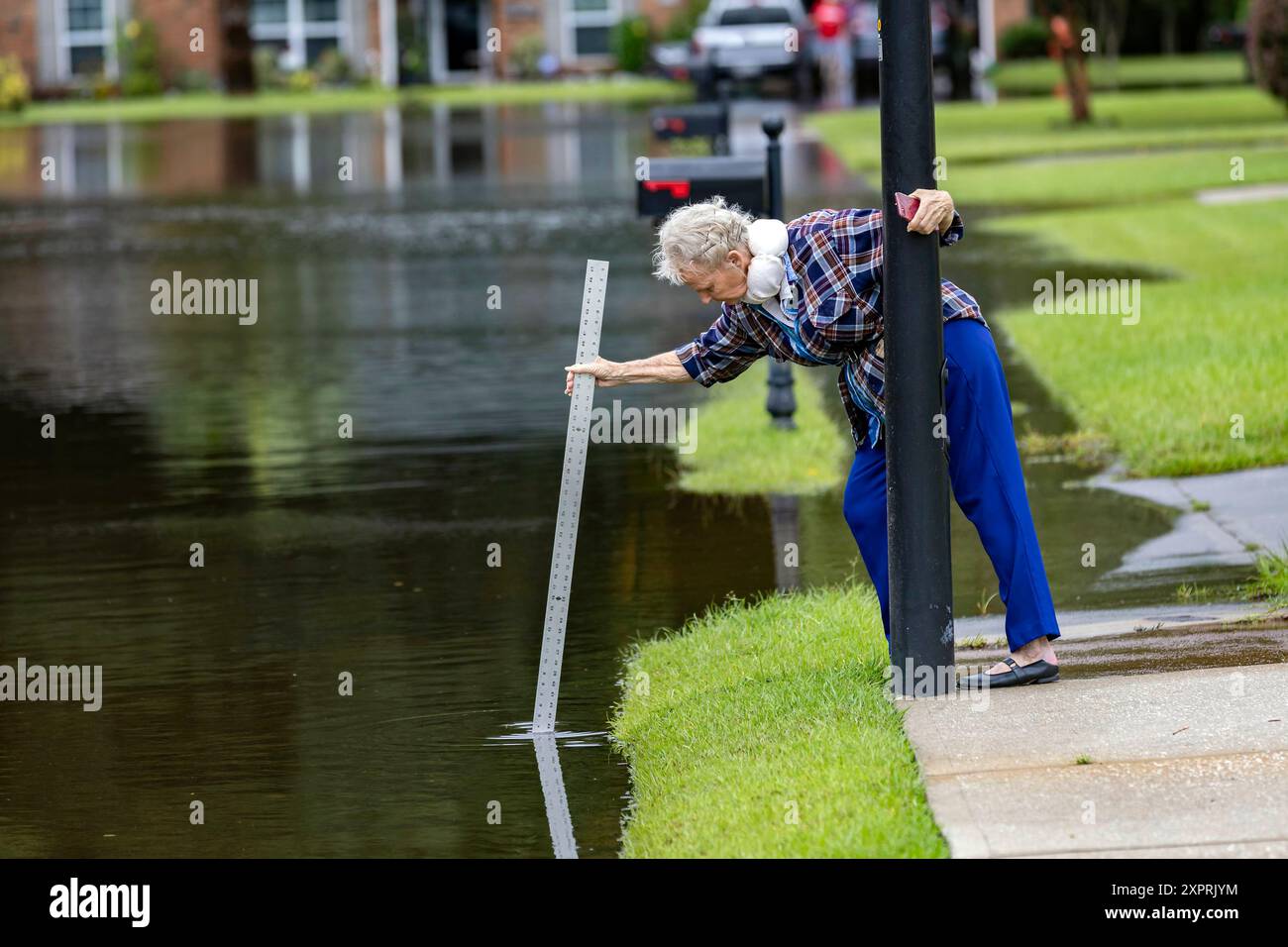 A resident measures the depth of the flooded street with storm water ...