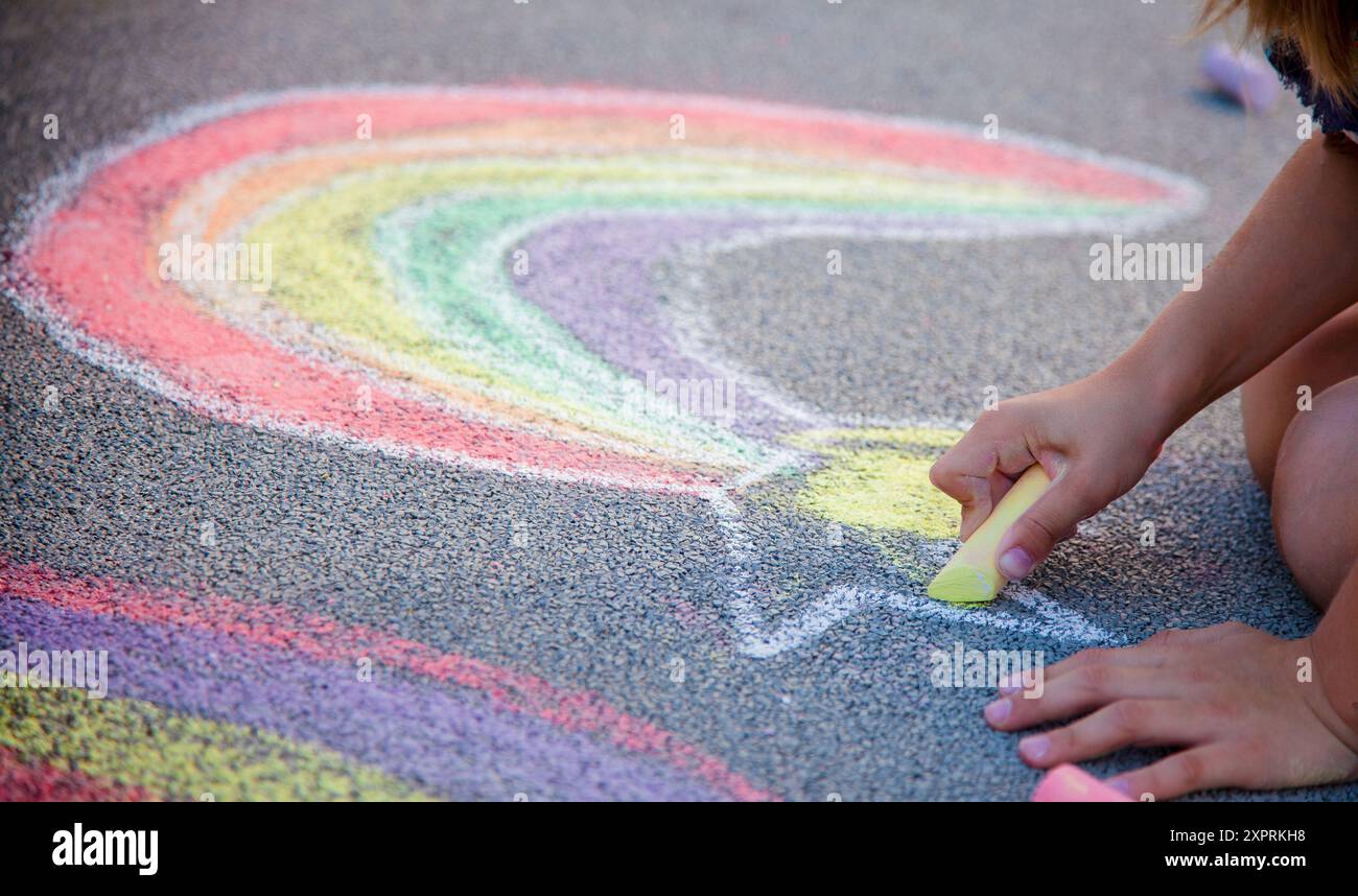 Children draw a rainbow on the asphalt with colored chalk. Sidewalk ...