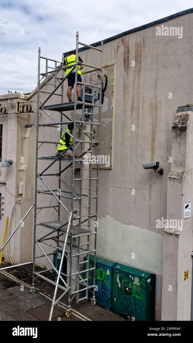 Two workmen on scaffolding mounting a transparent protective screen ...