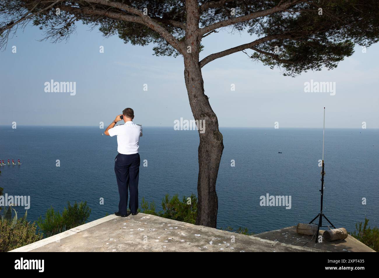 A border patrol officer stands on a platform under a tree, using ...