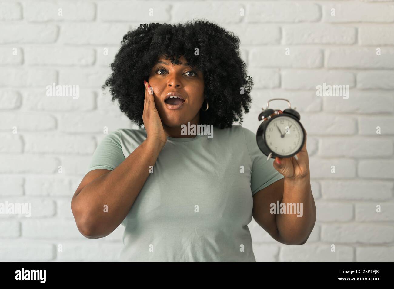 Surprised african american woman holding alarm clock amazed with open ...