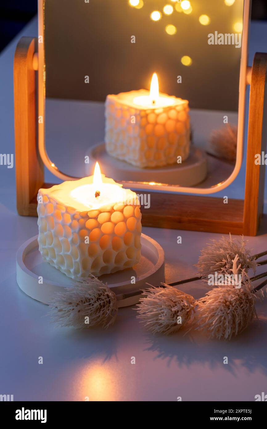 Lit cube handmade soy candle in front of a mirror with dried decorative ...