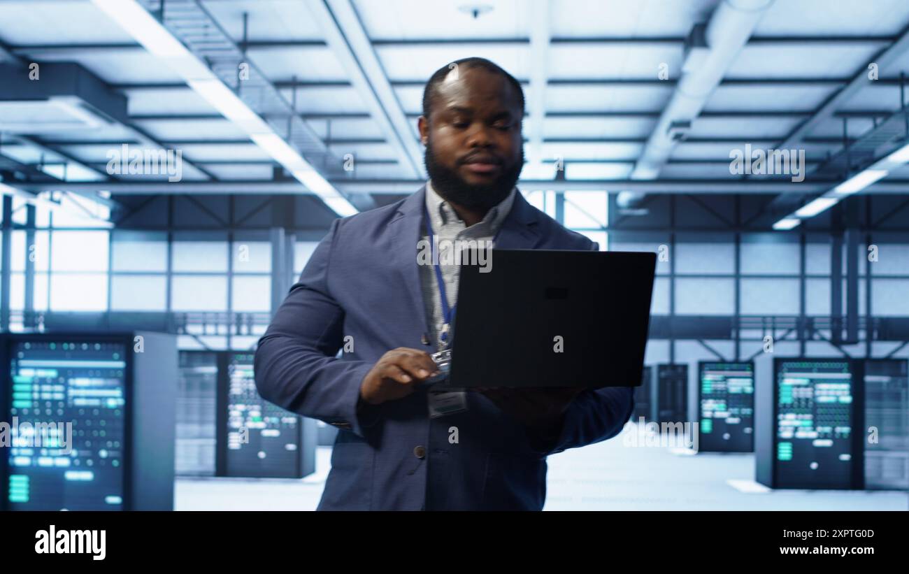 IT engineer working on laptop in modern data center, overseeing server ...