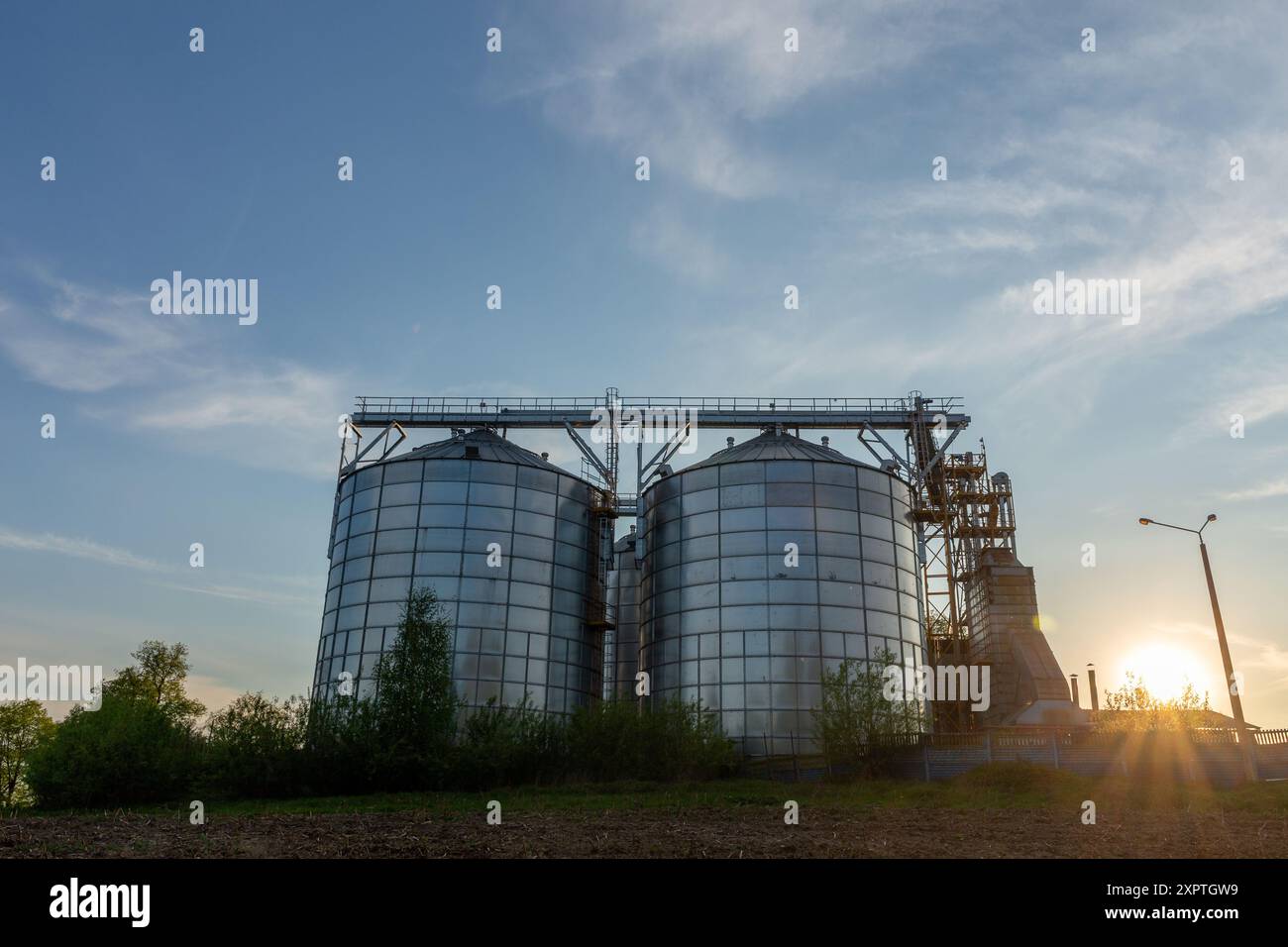 Agricultural silos next to harvested field in sunset . Set of storage ...