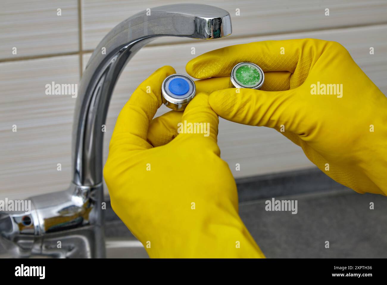 Replacing a clogged kitchen sink faucet aerator. Hands in yellow rubber ...