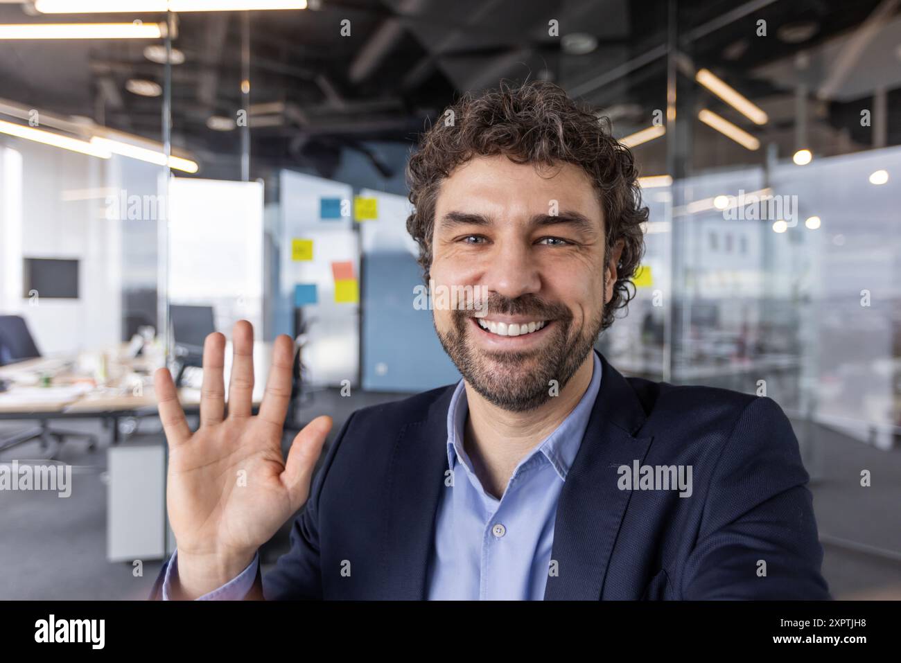 Happy businessman waving looking at camera during video call in modern ...