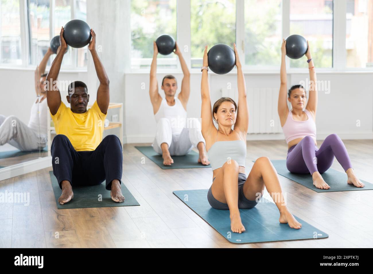 Girl conducts Pilates class for multinational group sitting with soft ...