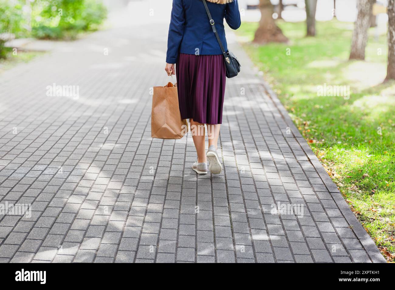 Back view of a woman carrying a brown paper shopping bag, walking on a ...