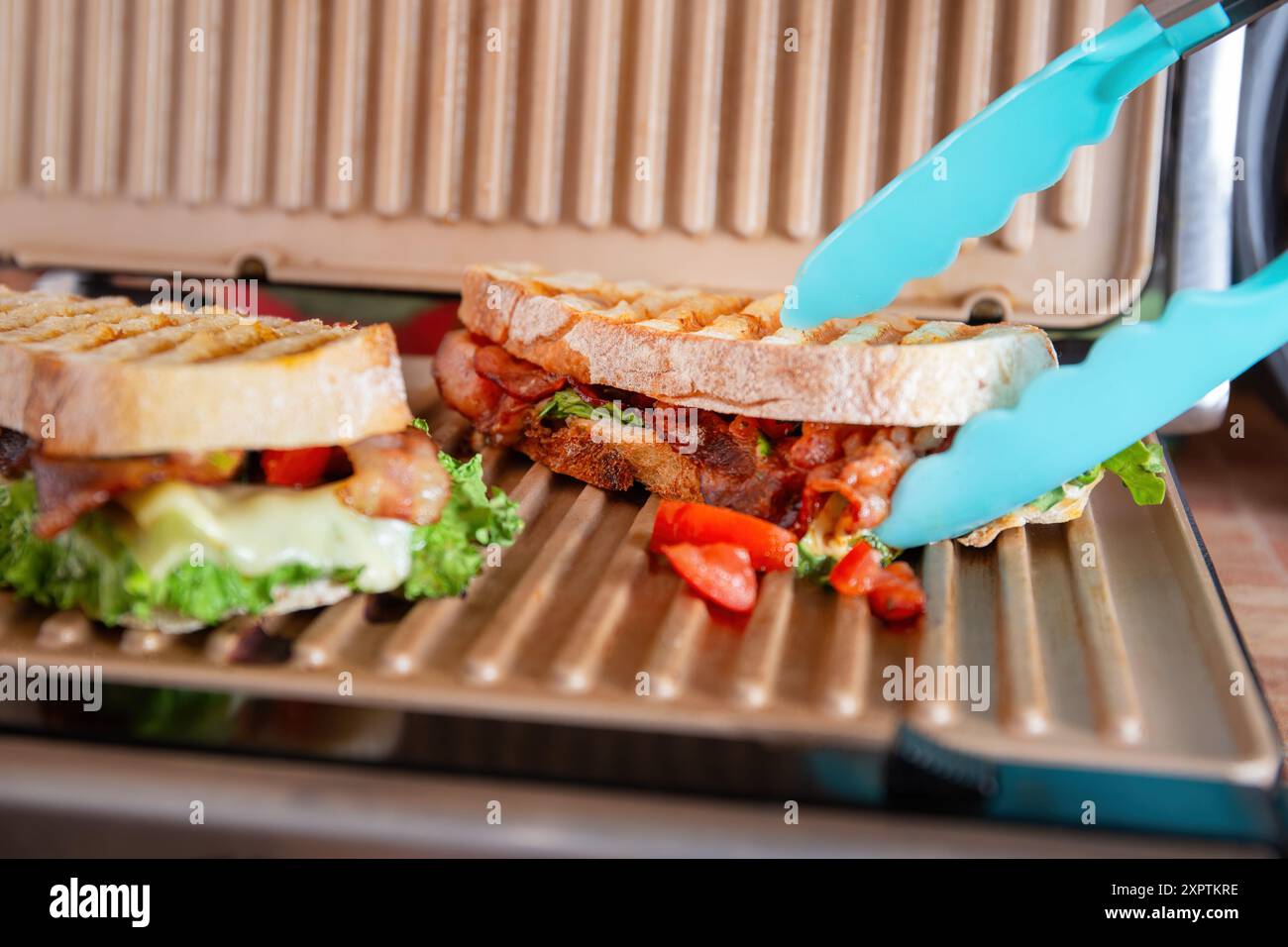 Two grilled sandwiches with bacon, lettuce, and tomatoes cooking on a ...