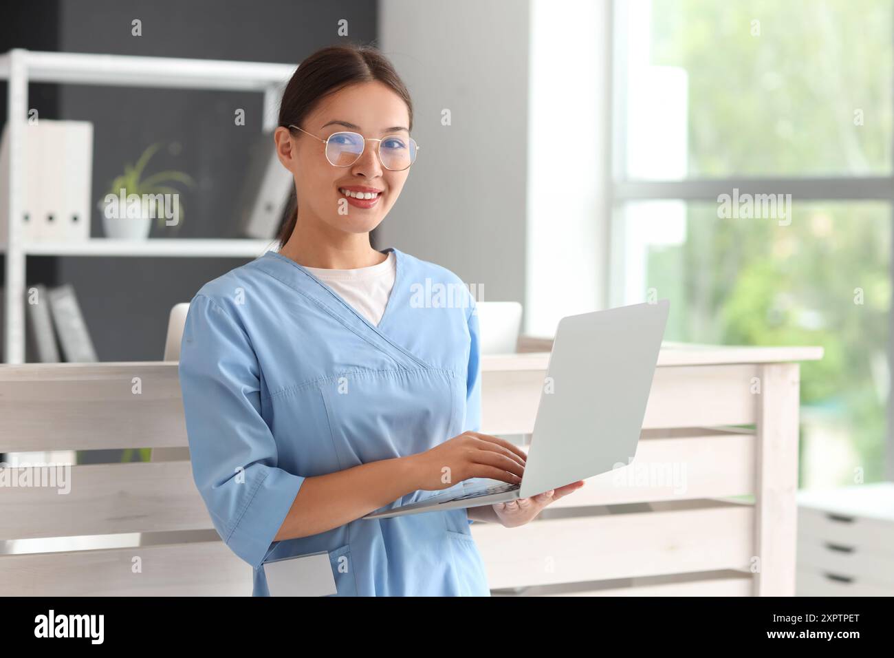 Young female medical receptionist in eyeglasses with modern laptop in ...