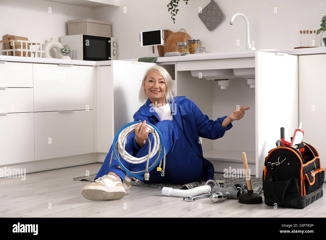 Mature female plumber with pipes pointing at sink in kitchen Stock ...