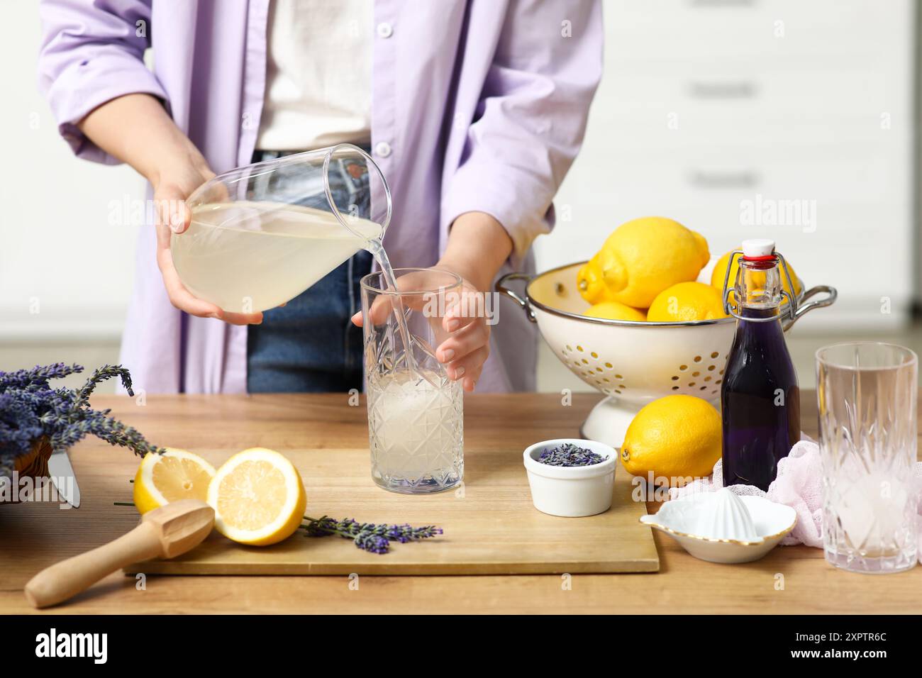 Young woman pouring lemon juice from jug into glass for preparing ...