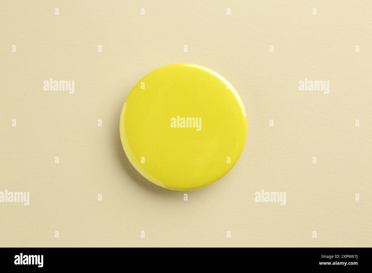 Yellow button badge on beige background, top view. Mockup for design ...