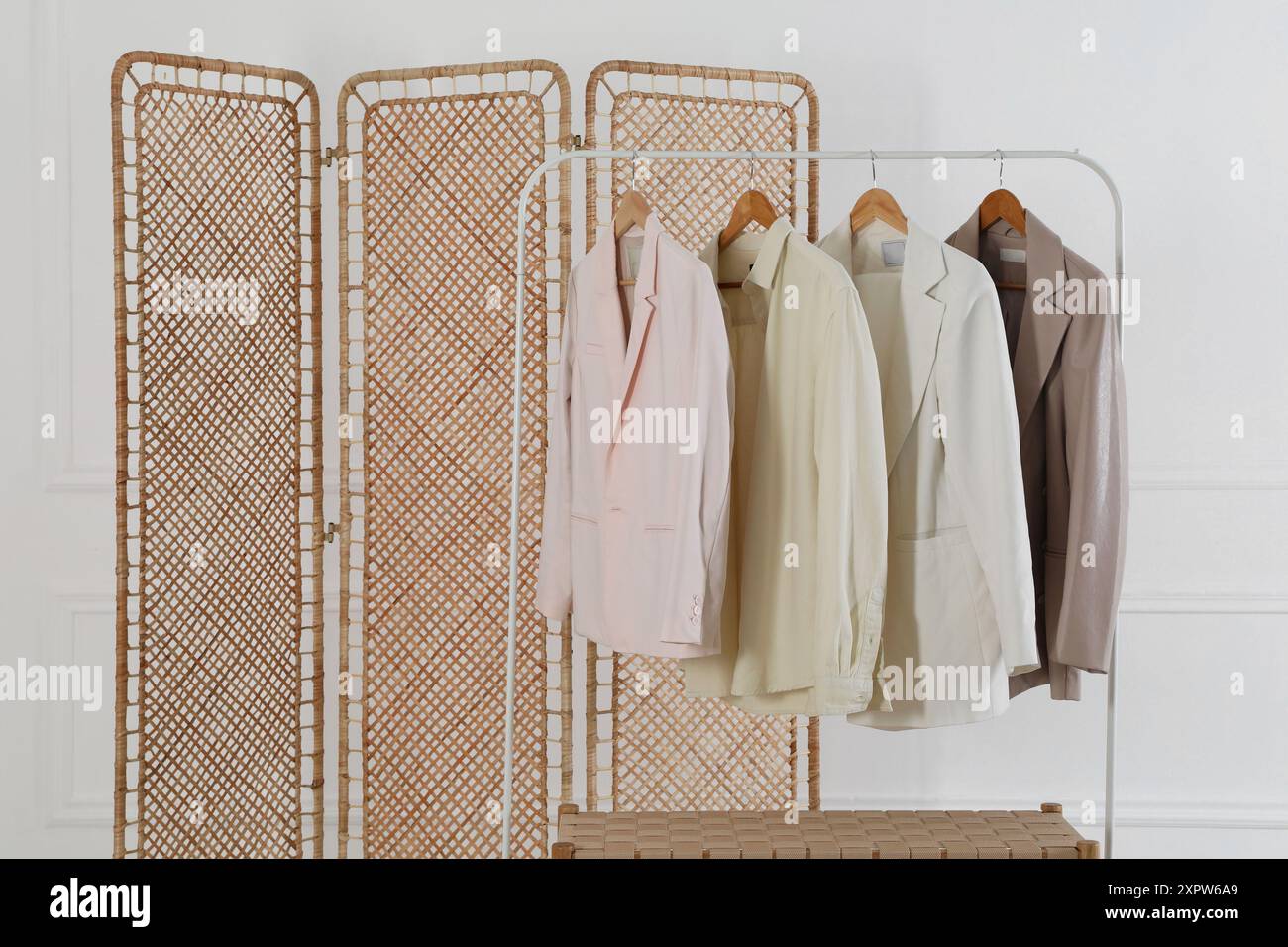 Folding screen, rack with clothes and storage bench near white wall ...