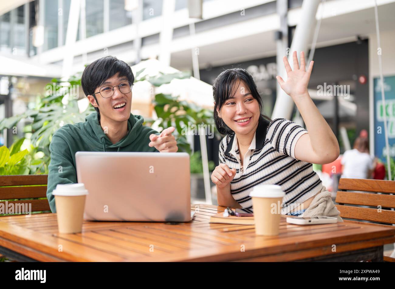 Two cheerful and friendly young Asian friends are sitting at a cafe ...