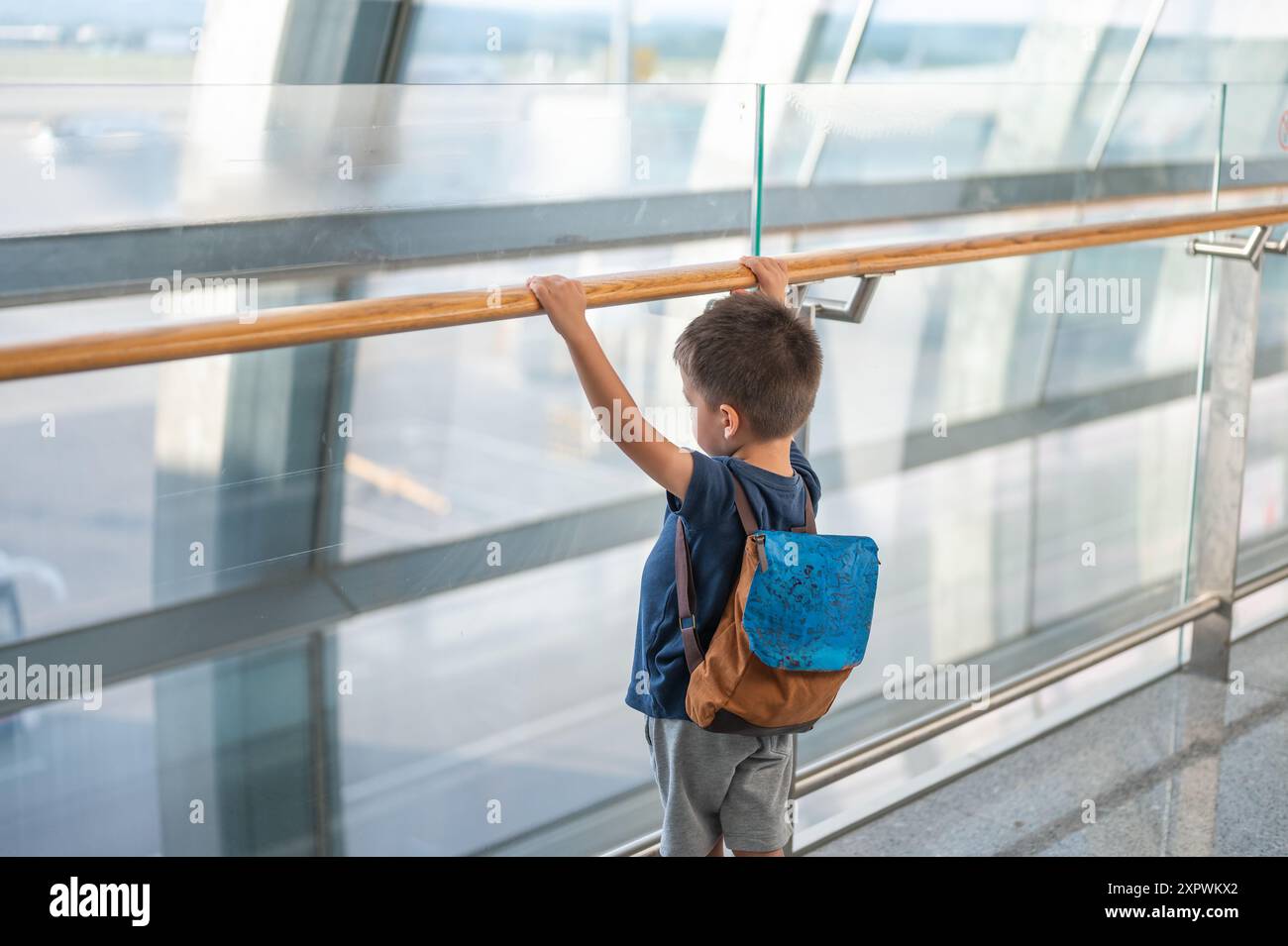 A young child with a colorful backpack stands by a railing and looks ...