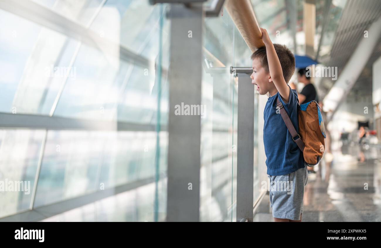 A young child, wearing a backpack and shorts, stands holding a railing ...