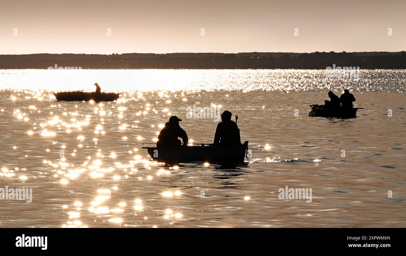 Three small fishing boats with silhouettes during early morning on lake ...