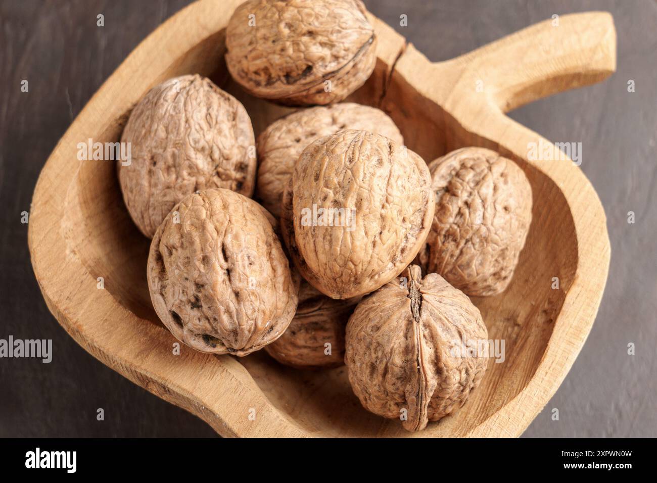 Ripe unshelled walnuts in shell in a shaped wooden craft bowl. Unpeeled ...