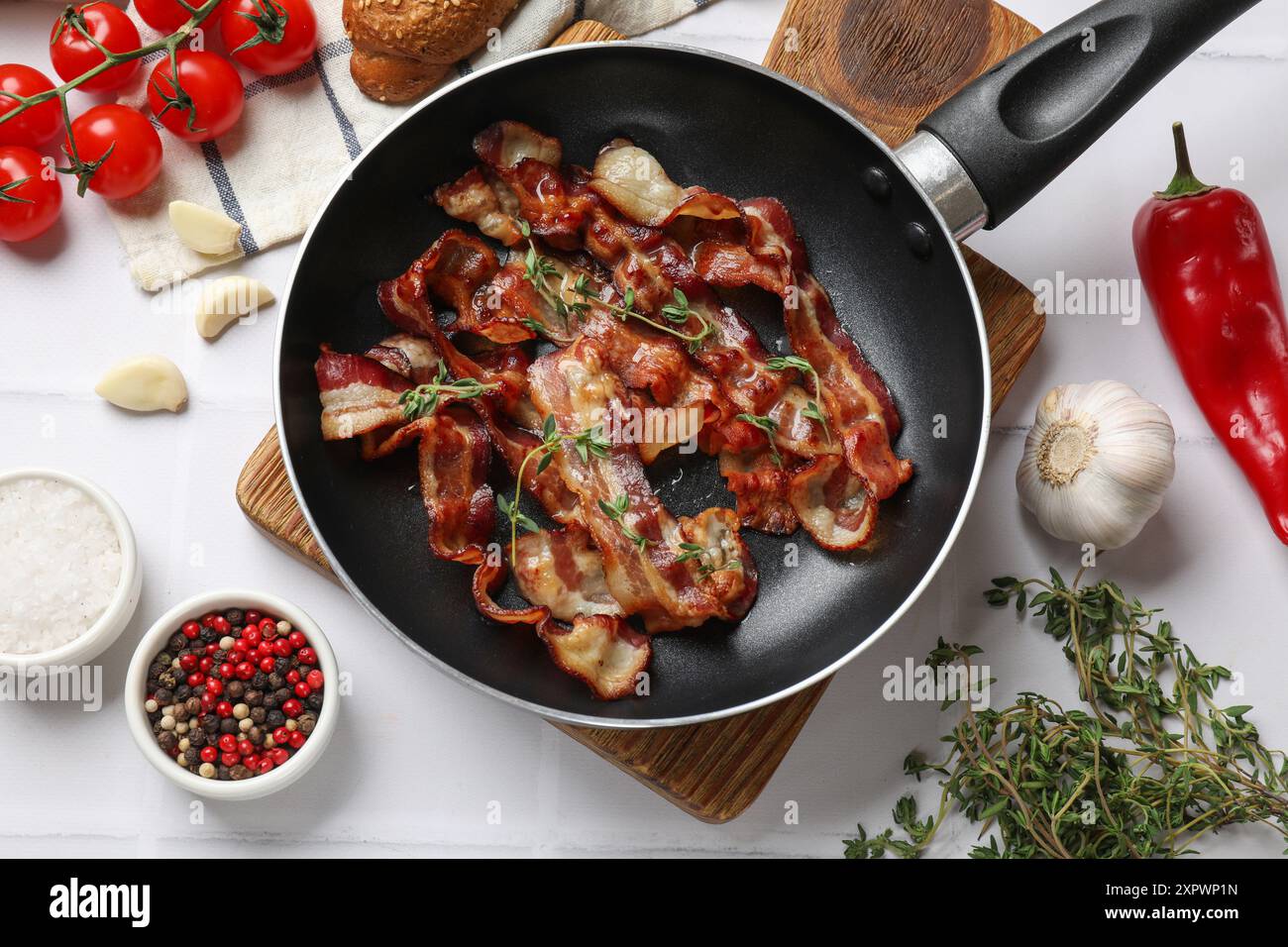 Delicious bacon slices in frying pan and products on white tiled table ...