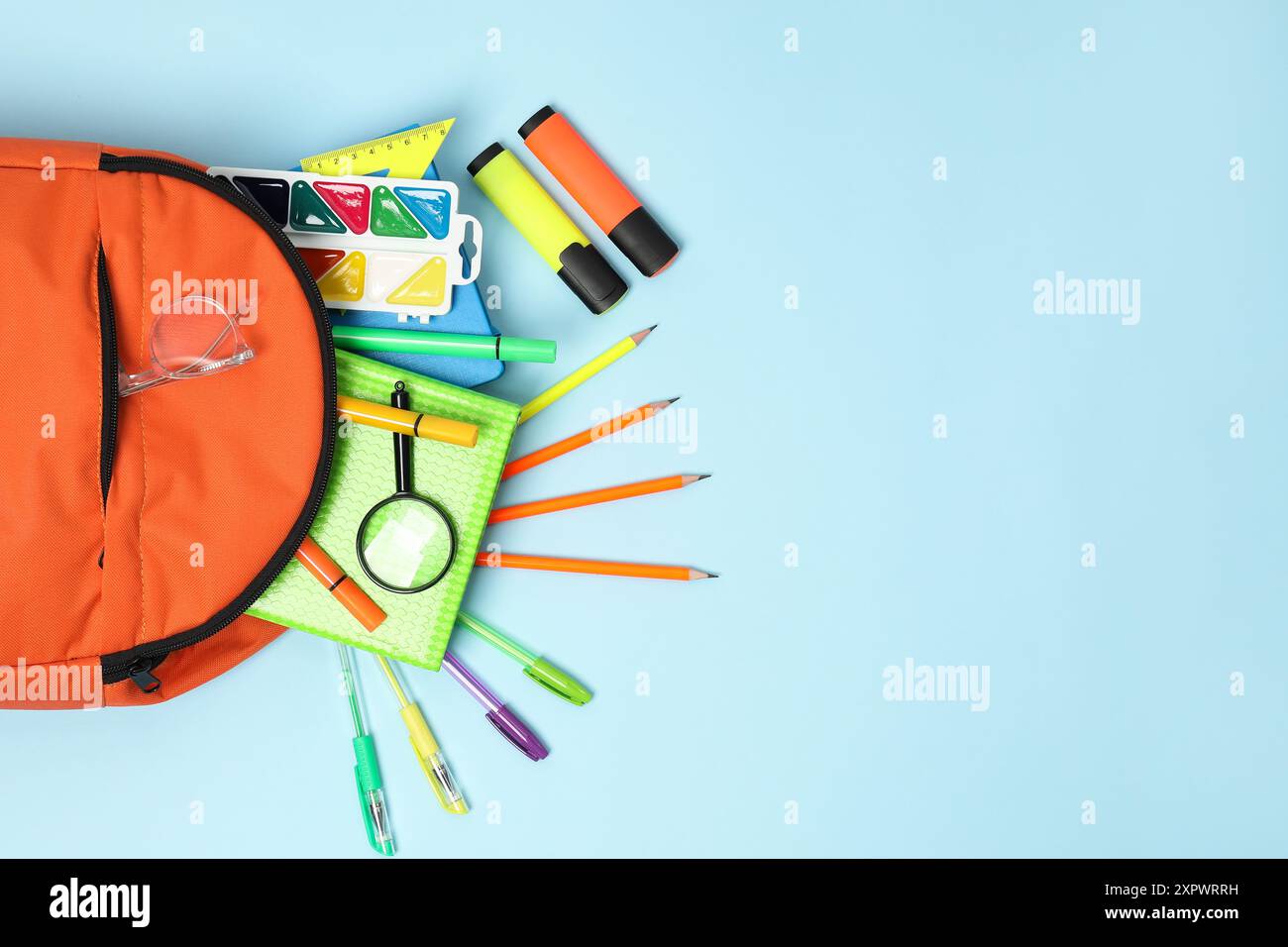 Orange backpack and different school supplies on light blue background ...