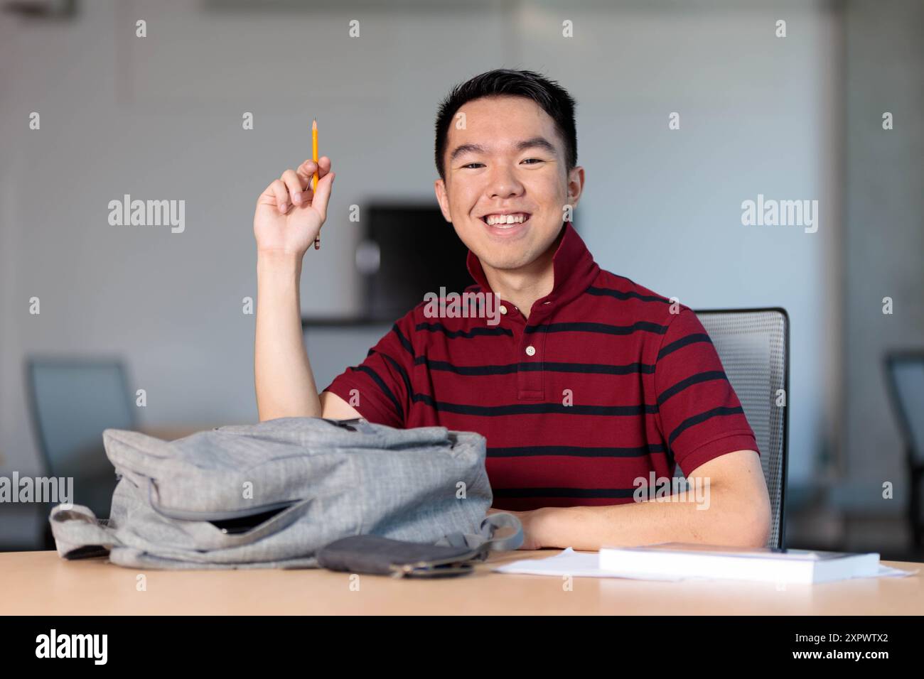 A young teenage college student is sitting at a table with his backpack ...