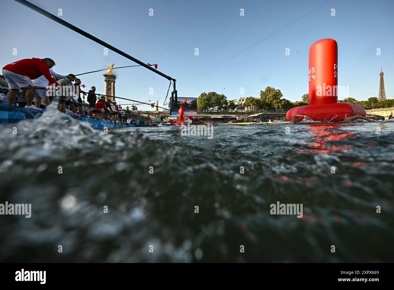 Team members use poles to extend hydration bottles to athletes as they ...