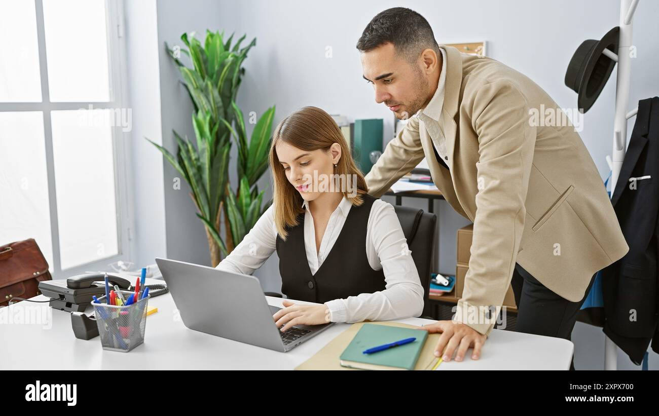 A professional man and woman collaborate using a laptop in a modern office setting, discussing ...