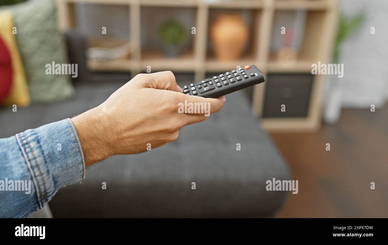 A close-up of a man's hand holding a remote control in a modern living ...