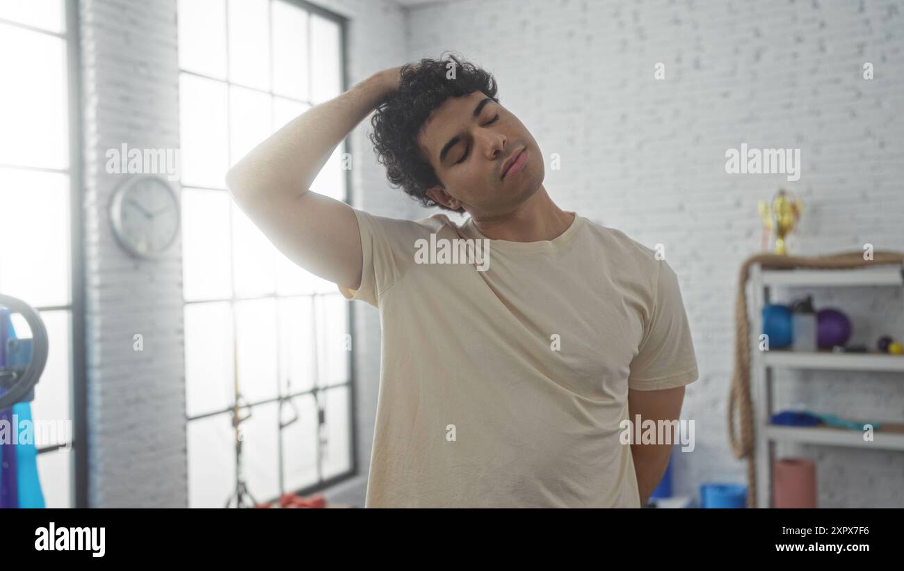 Handsome, young, hispanic man stretching in an indoor gymnasium ...