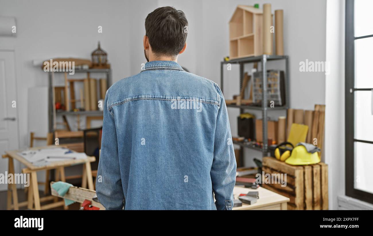 Back view of a young man in a denim jacket standing in a bright ...