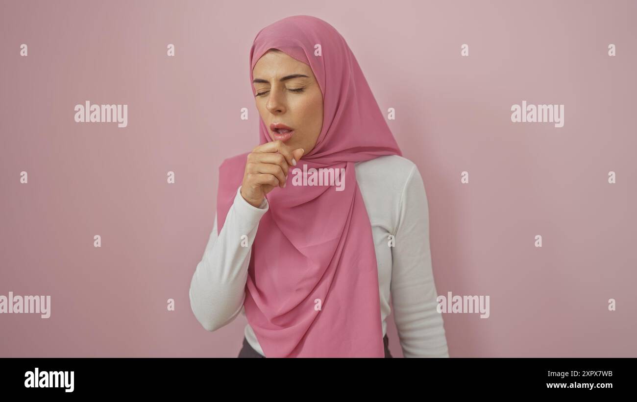 A young muslim woman in a pink hijab coughing against an isolated pink ...