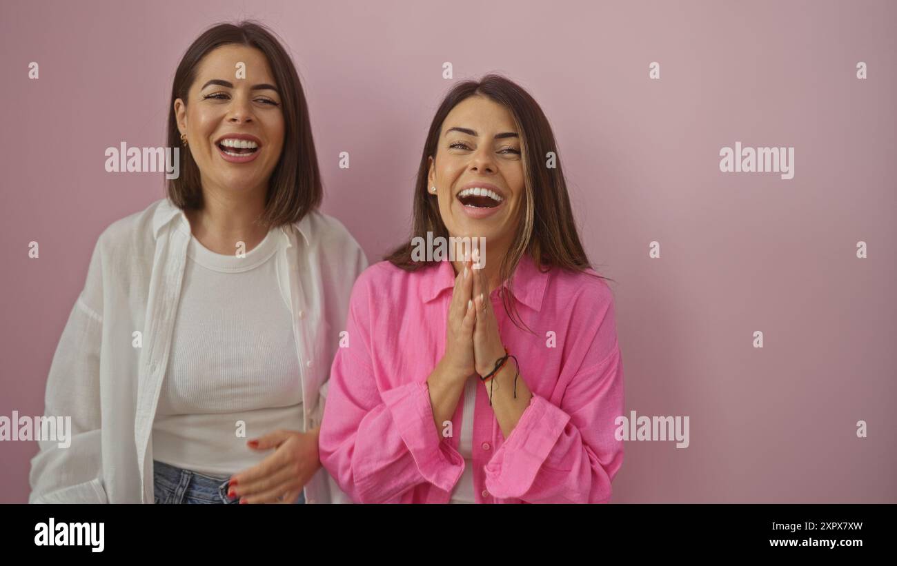 Two women laugh together against a pink background, displaying a joyful ...