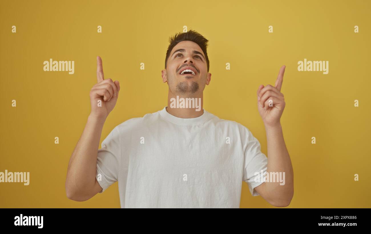 Handsome young man pointing upwards, isolated on a yellow background ...