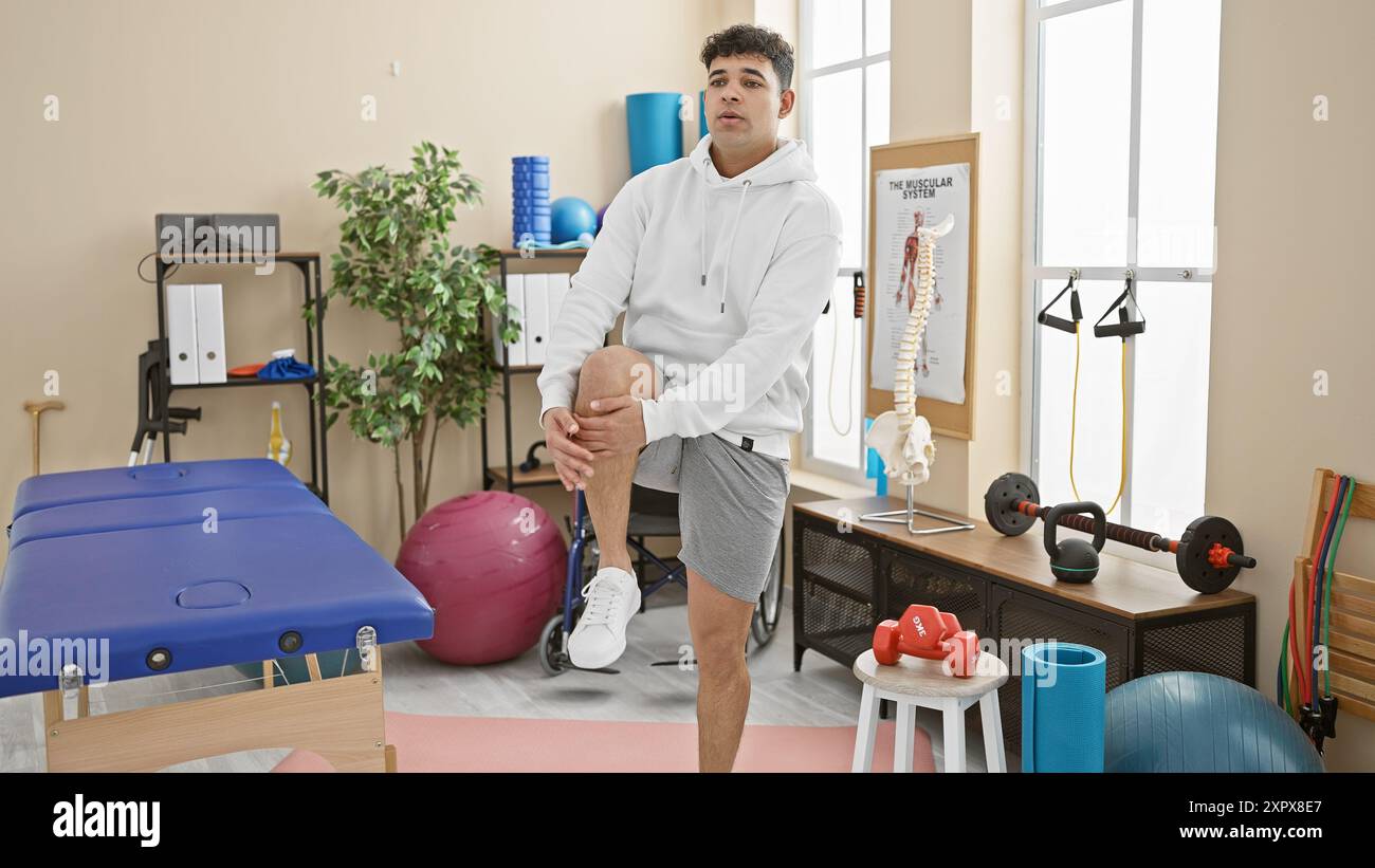 A young man stretches in a well-equipped physiotherapy clinic with ...