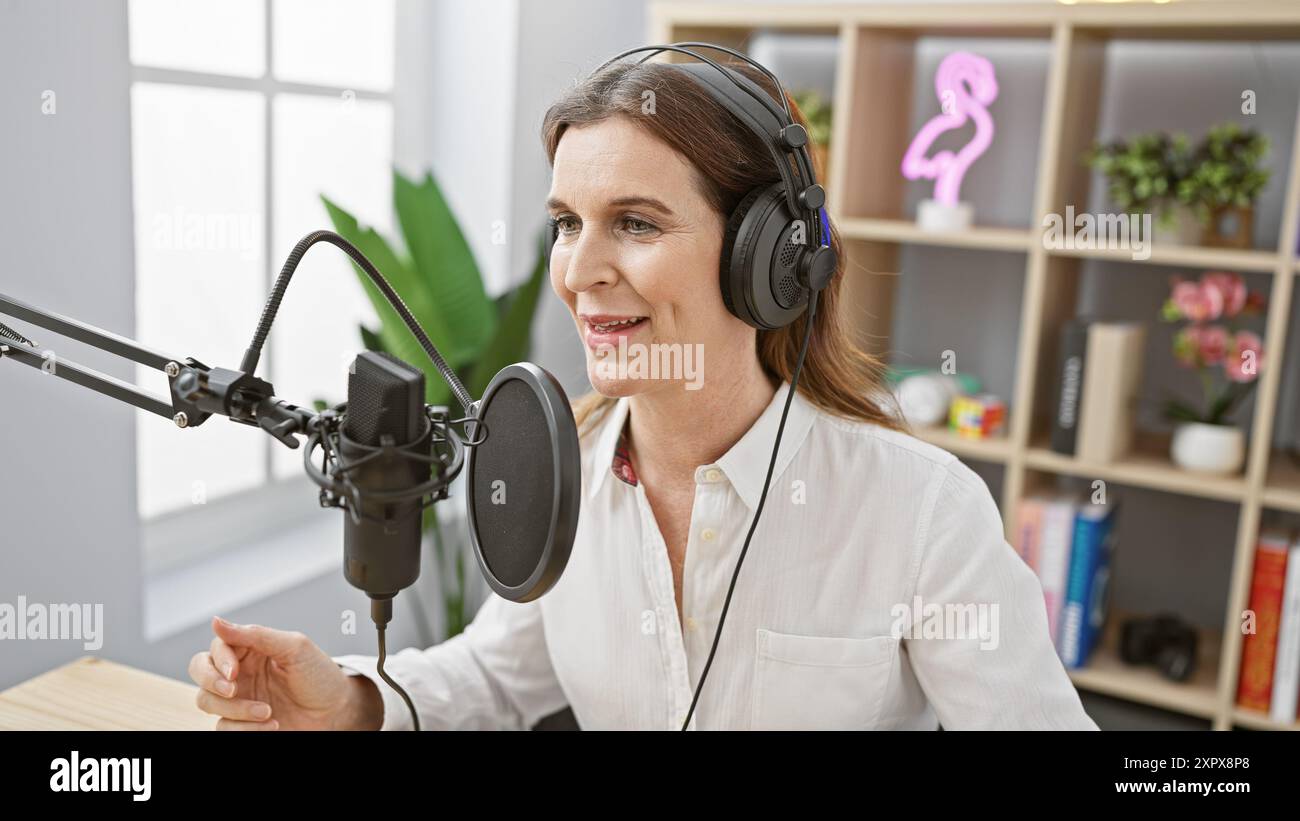Middle-aged woman in headphones speaking into microphone in a podcast studio setup Stock Photo ...