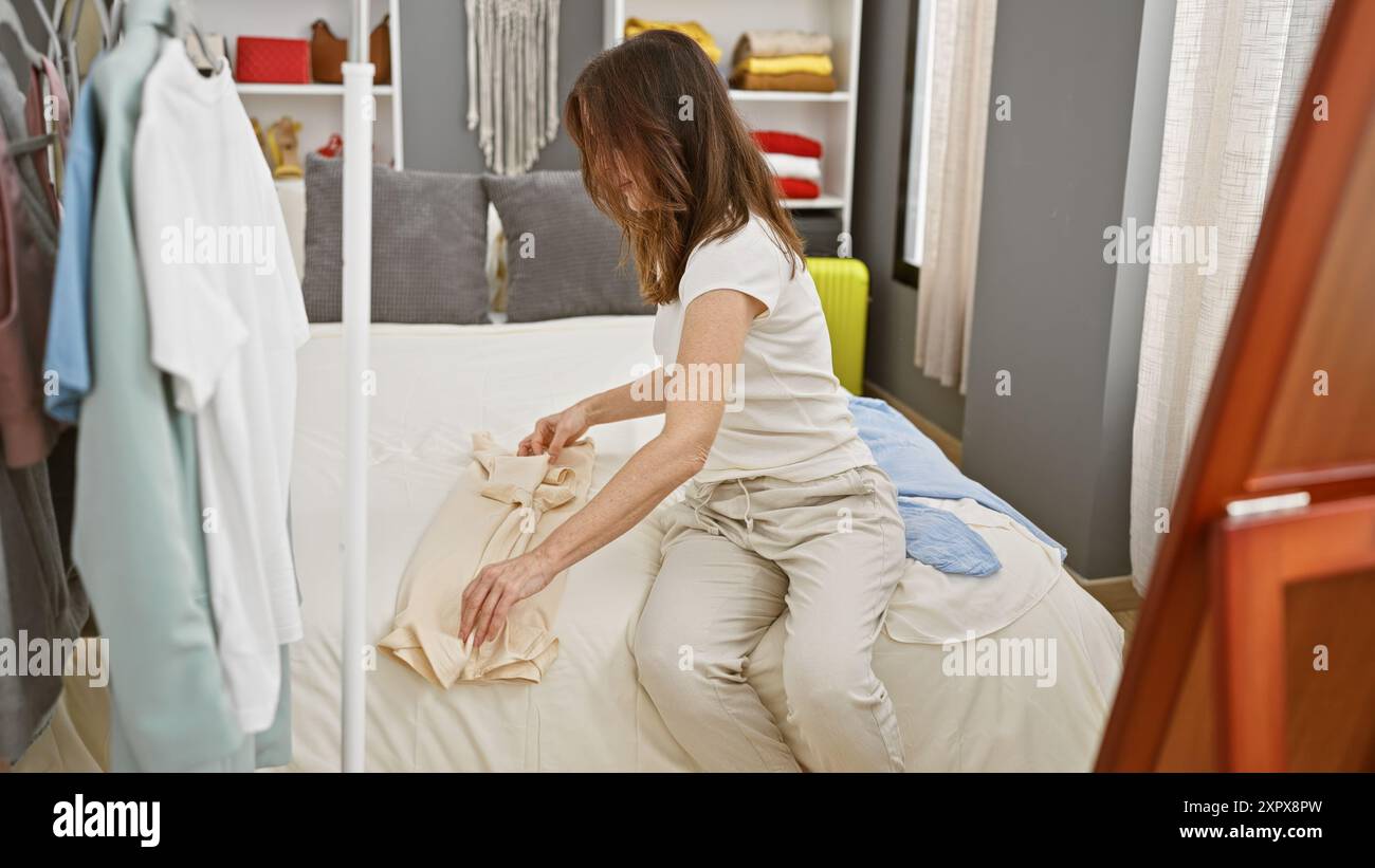 Mature woman folds clothes in a bright bedroom with an open wardrobe ...