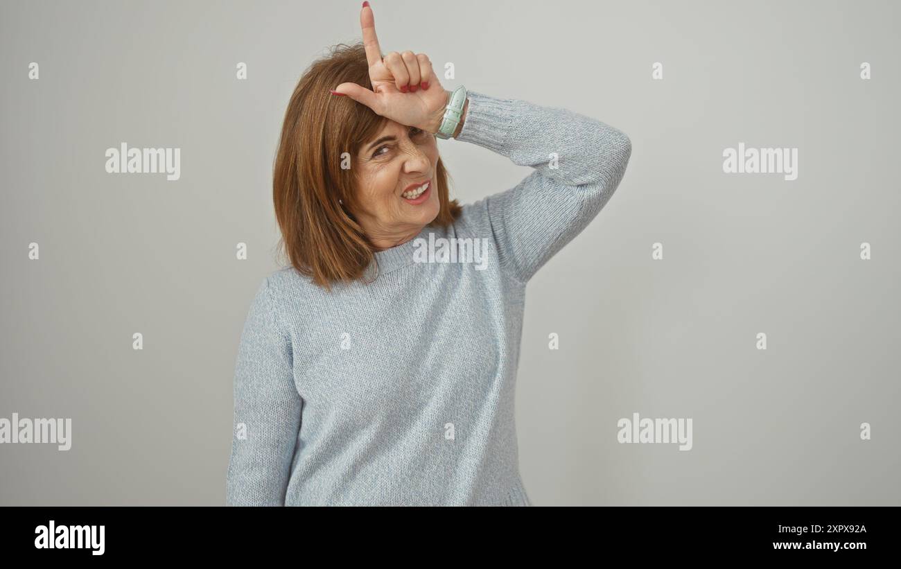 A playful mature woman gesturing 'loser' sign against a white wall ...